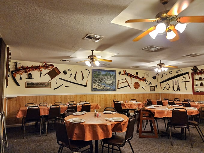 Vintage farm tools adorn walls above orange-clothed tables, creating a museum of rural Americana where the main exhibit is your soon-to-arrive feast.