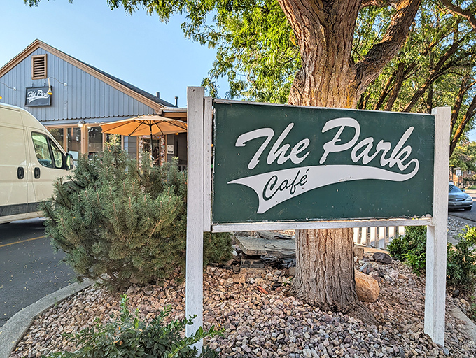 Beneath towering trees, The Park Cafe's inviting sign and outdoor seating promise a breakfast experience worth writing home about.