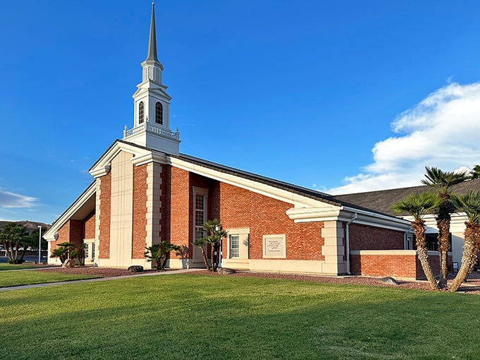 The Church of Jesus Christ of Latter-day Saints rises gracefully under a bright blue sky, its white steeple and red brick glowing with quiet dignity.