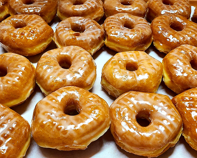 Golden-hued glazed donuts glisten under the display lights, their perfect sheen promising that satisfying first bite that makes your eyes close involuntarily.
