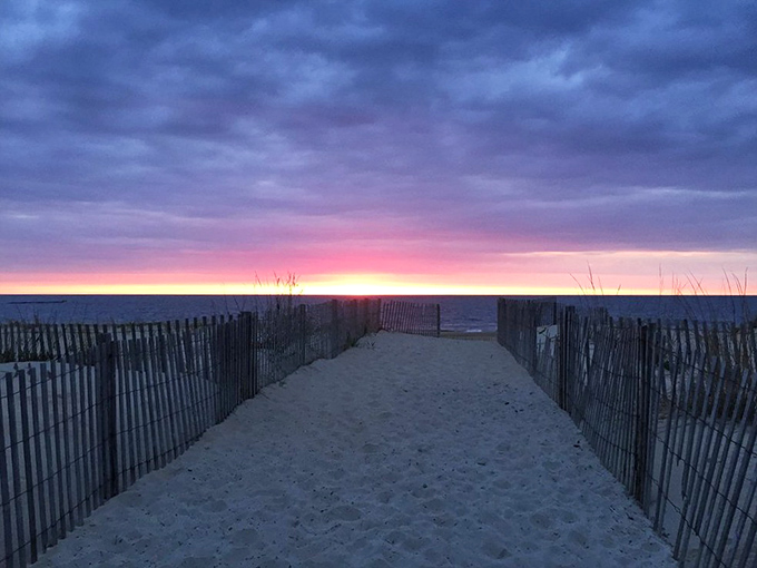 A sandy pathway flanked by weathered fences invites beachgoers toward the promise of Atlantic waves ahead.