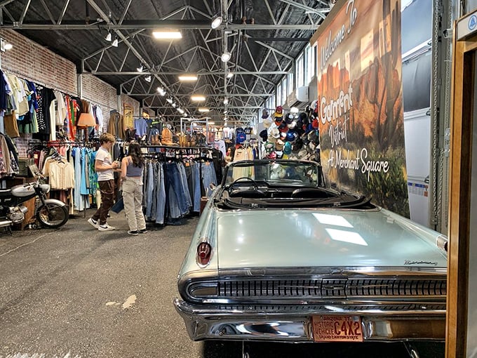 A mint-condition classic convertible sits proudly among racks of vintage clothing, proving some treasures have four wheels and chrome bumpers.