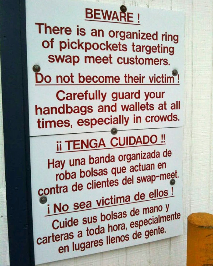 Even paradise comes with warnings! This bilingual sign reminds swap meet treasure hunters to keep their valuables close.