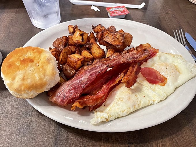 The breakfast trinity: perfectly cooked eggs, crispy bacon, and golden home fries alongside a biscuit that would make your grandmother jealous.