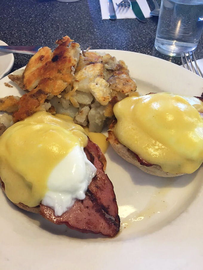 Behold the star attraction: eggs Benedict with golden hollandaise cascading down like a sunrise, perfectly poached eggs, and home fries that deserve their own fan club.