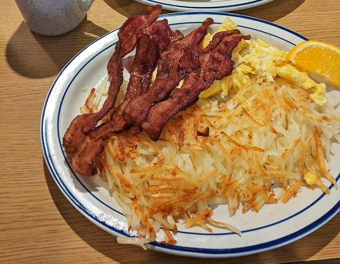 Crispy hash browns and perfectly cooked bacon frame eggs that would make a chicken proud – simple breakfast perfection on a blue-rimmed plate.