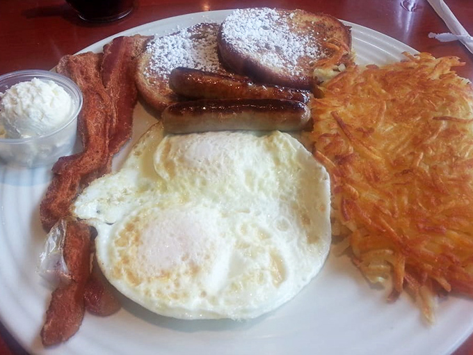 Breakfast perfection on a plate: golden French toast dusted with powdered sugar, crispy bacon, a sunny-side egg, and hash browns that could make a potato weep with pride.