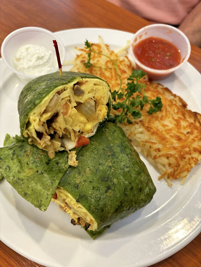 Behold the legendary breakfast burrito in its green spinach wrap glory, served with hash browns that deserve their own fan club.