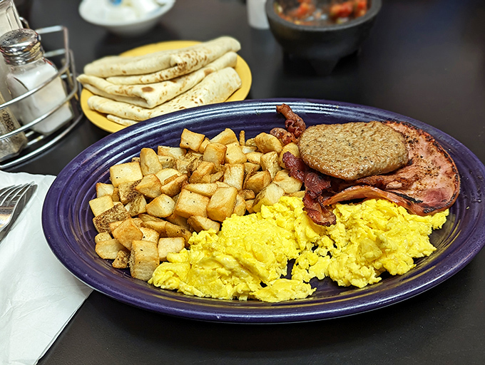 Breakfast perfection on a purple plate: golden scrambled eggs, crispy potatoes, and bacon with tortillas standing by. The holy trinity of morning satisfaction.