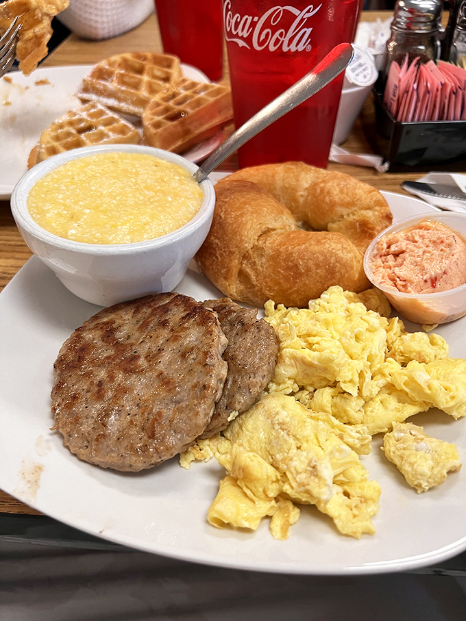 Breakfast nirvana on a plate: fluffy scrambled eggs, sausage patty, grits, and a croissant that would make a French baker nod in approval.