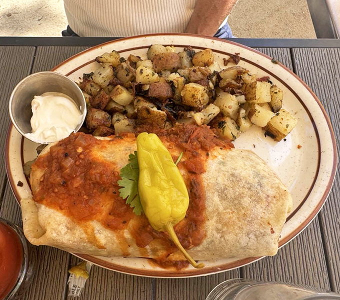 This breakfast burrito isn't just food&mdash;it's edible architecture, with perfectly seasoned potatoes standing guard beside a tortilla-wrapped masterpiece topped with that legendary ranchero sauce.