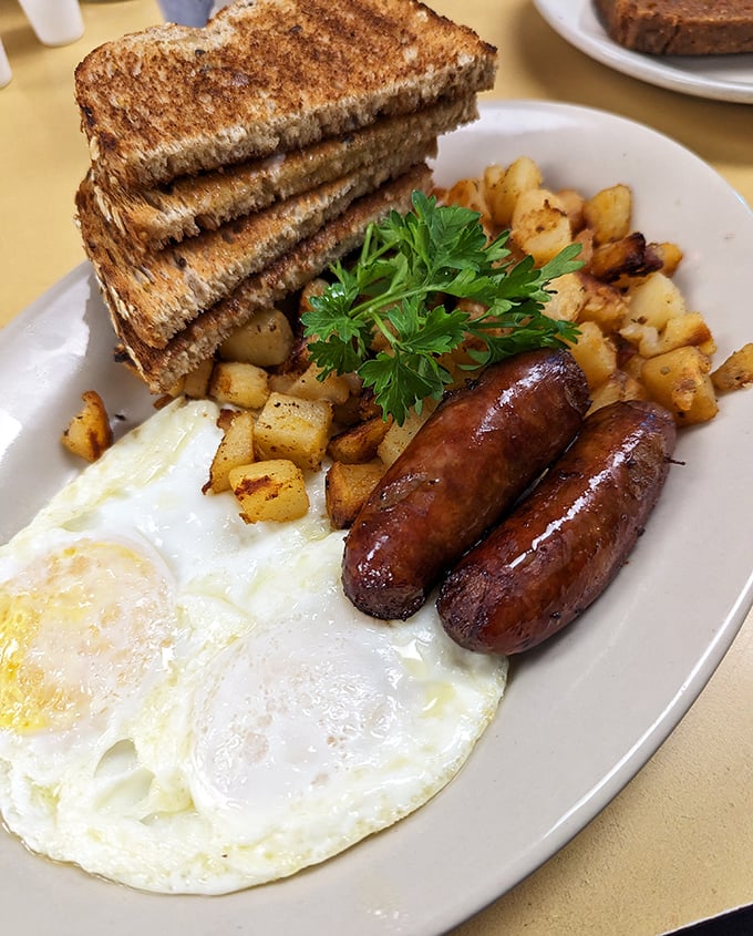 Breakfast perfection on a plate: golden-brown toast, home fries with just the right crisp, sausage links that snap, and eggs sunny-side up smiling at you.
