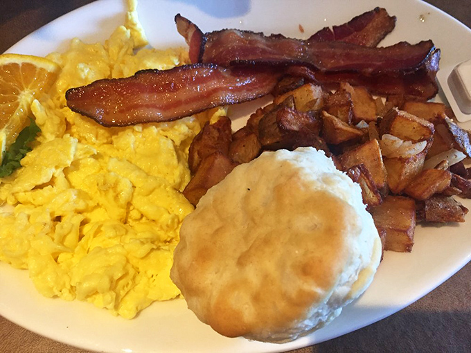 Breakfast nirvana on a plate: golden scrambled eggs, perfectly crisped bacon, and a biscuit so fluffy it might float away if not for gravity's intervention.
