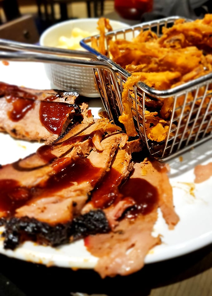 Brisket so tender it practically surrenders to your fork, with a smoke ring that would make Texas pitmasters nervously check their smokers. 