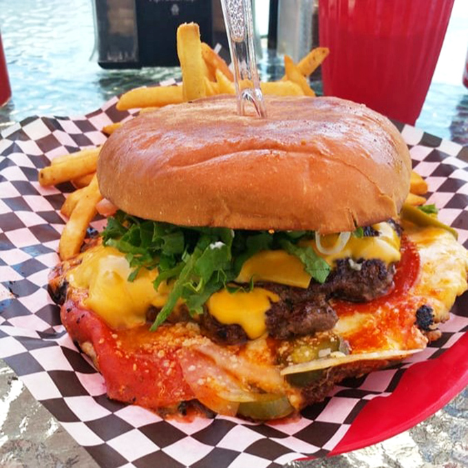 Behold the burger in its natural habitat: juicy, cheese-draped, and nestled on a checkered paper throne. That knife isn't decoration&mdash;it's structural support. 