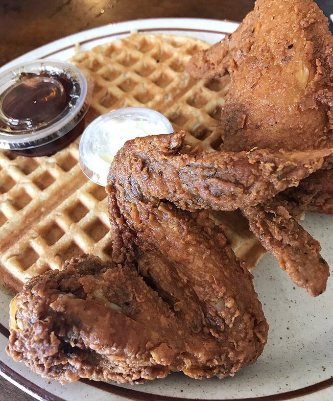 Behold the star attraction: golden-brown fried chicken perched atop a perfect waffle, with syrup and butter standing by for their supporting roles.