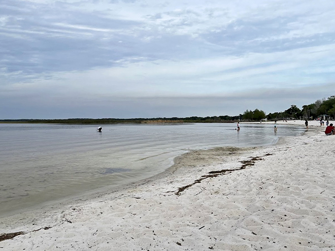 Gentle waves lap against pristine shores where families wade in tea-colored waters without a tourist in sight.