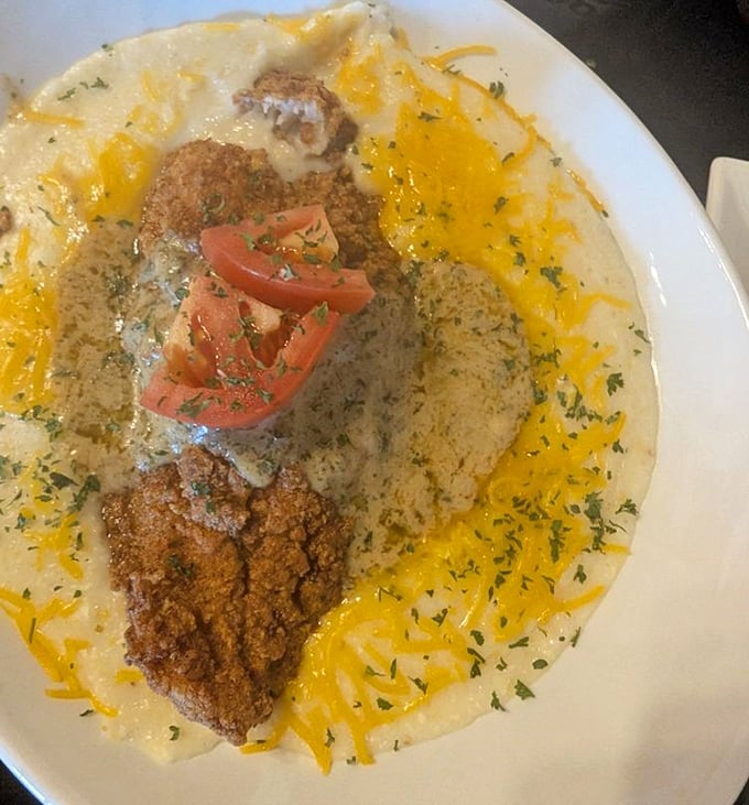 Creamy grits cradle perfectly seasoned catfish like a Southern lullaby, with shredded cheese and fresh tomatoes adding pops of color and flavor.