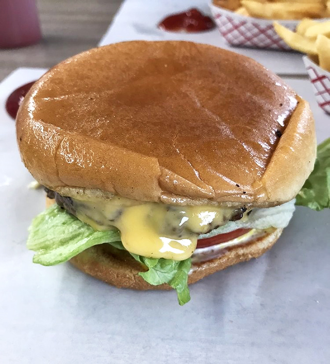 Behold the star attraction: a perfectly proportioned cheeseburger where the melted cheese cascades over the patty like a dairy waterfall of dreams.