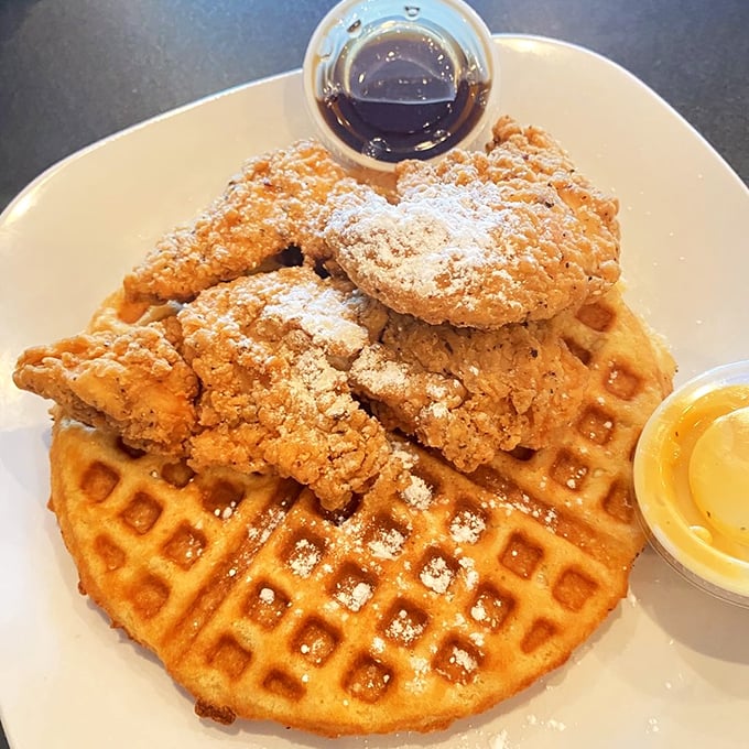 Behold the headliner: golden-fried chicken atop a Belgian waffle throne, dusted with powdered sugar like fresh Tennessee snow.
