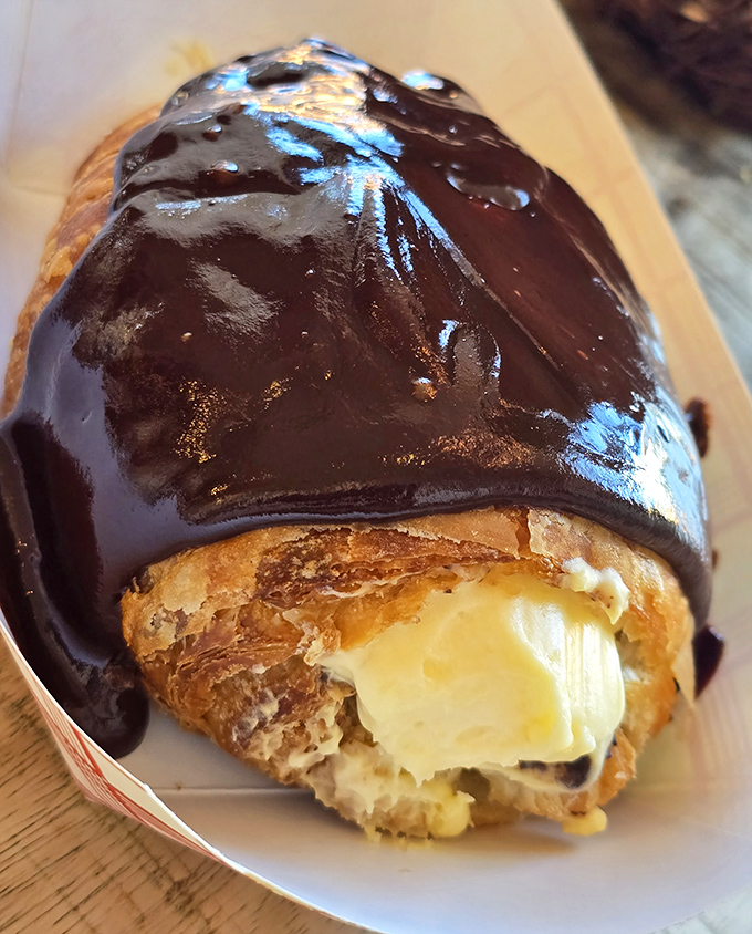 This chocolate-dipped eclair isn't just a pastry—it's a commitment to excellence. The custard filling peeks out like it's playing hide and seek.