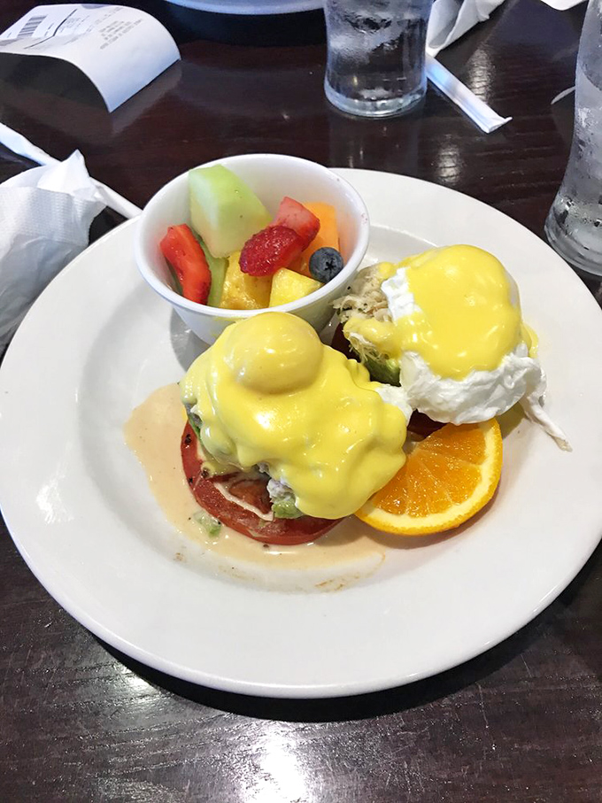 Behold the star of our show: Eggs Benedict with perfectly poached eggs wearing hollandaise like a couture gown, accompanied by fresh fruit that didn't come from a can.