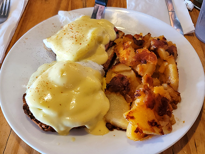Behold the star attraction: Eggs Benedict with hollandaise cascading like golden waterfalls over perfectly poached eggs alongside crispy home fries.