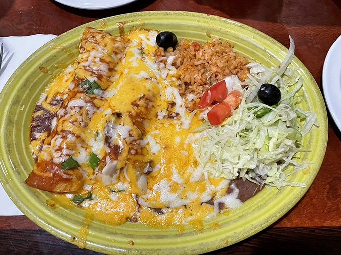 Cheese-blanketed enchiladas bask on a sunshine-yellow plate, flanked by Spanish rice and a fresh salad—a holy trinity of satisfaction.