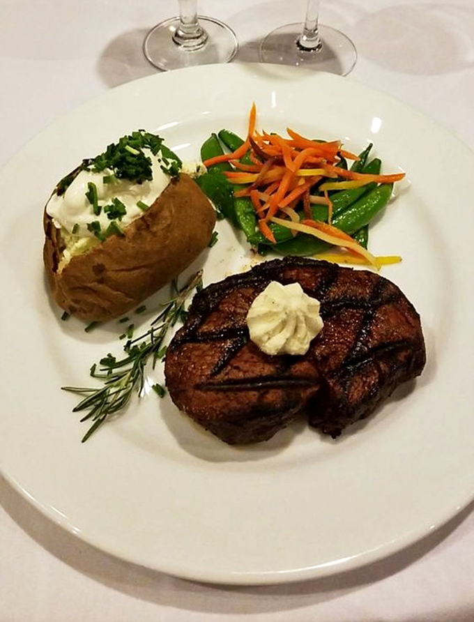 Behold the filet mignon in its natural habitat &ndash; perfectly seared, topped with herb butter, and flanked by a loaded baked potato that's practically begging to be devoured.