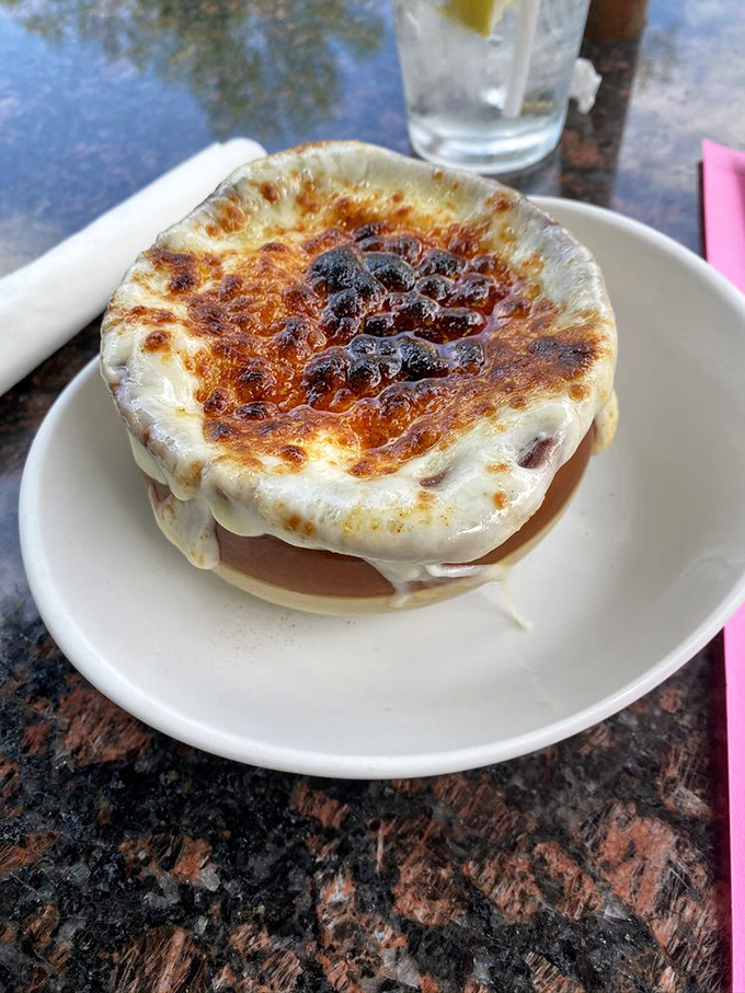The French onion soup arrives like a cheese volcano that erupted in heaven &ndash; that perfect golden dome hiding a savory treasure worth every stretchy, messy bite.