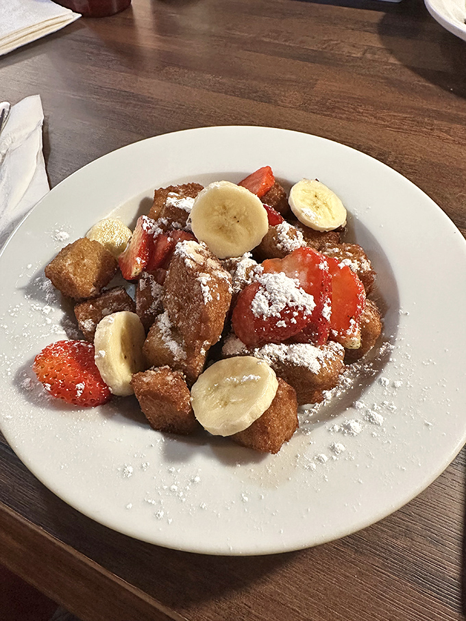 Behold the legendary Three Brothers Style French Toast! Those golden cubes mingling with fresh strawberries and bananas under a snowfall of powdered sugar – breakfast doesn't get more photogenic.