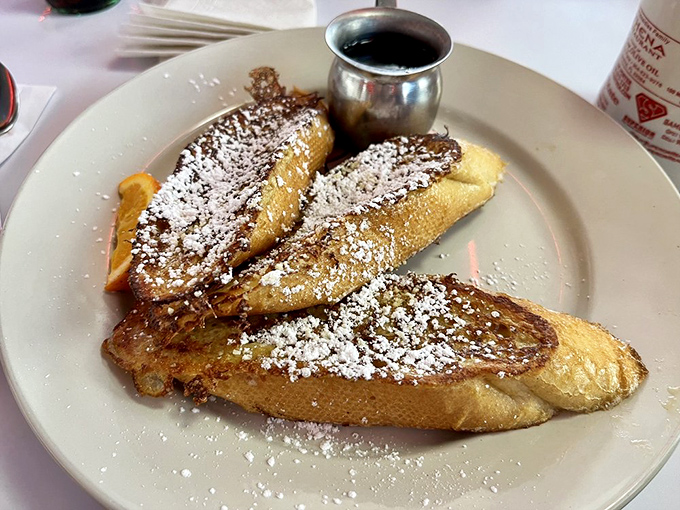 This French toast doesn't just arrive at your table—it makes an entrance, dusted with powdered sugar and accompanied by a silver pitcher of maple syrup standing at attention.