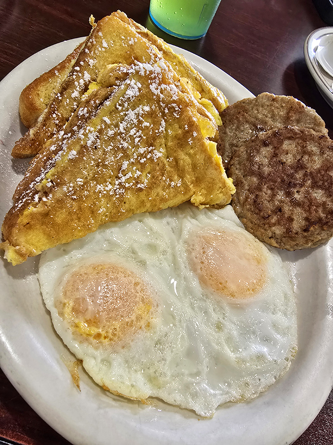 The legendary French toast arrives dusted with powdered sugar, flanked by perfectly cooked eggs and sausage &ndash; breakfast's holy trinity.