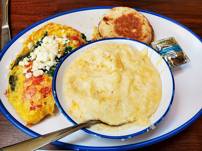 The star of the show: a perfectly executed Greek omelet with vibrant spinach and feta, accompanied by creamy grits and an English muffin.
