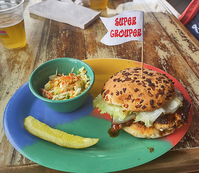The legendary Super Grouper Sandwich arrives like seafood royalty, complete with a tiny flag crown and the perfect companions of coleslaw and pickle.