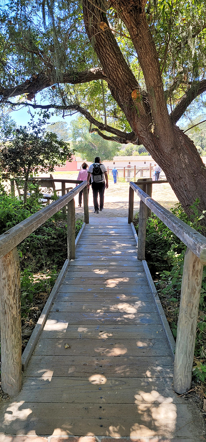 Nature's welcome mat to La Purisima Mission. This wooden bridge leads visitors through dappled sunlight toward California's most extensively restored mission.