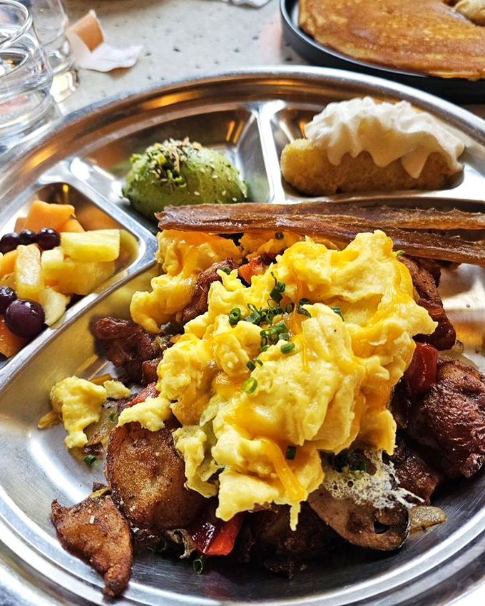 Breakfast alchemy at its finest&mdash;scrambled eggs nestled atop crispy potatoes with a supporting cast of fresh fruit and avocado. Morning gold.