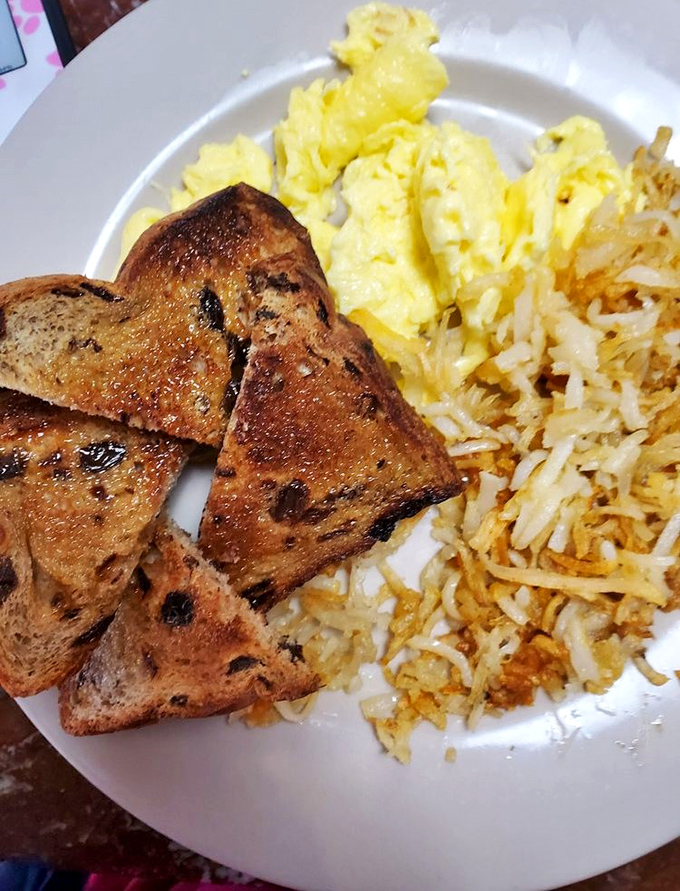 Breakfast perfection on a plate: golden-brown raisin toast, fluffy scrambled eggs, and hash browns with that ideal crisp-to-tender ratio. Morning salvation awaits.