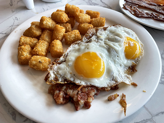 Breakfast perfection isn't complicated: two sunny-side-up eggs with crispy edges, golden tater tots, and sausage that snaps when you bite it. The holy trinity of morning salvation.