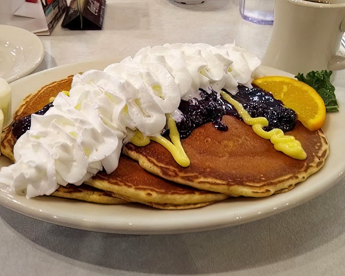Pancakes wearing whipped cream like a crown, with blueberry jewels and mustard-yellow sauce creating breakfast royalty on a plate.
