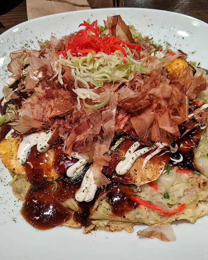 Okonomiyaki: Japan's answer to "what if pancakes went savory?" Topped with dancing bonito flakes that perform a little tableside show.