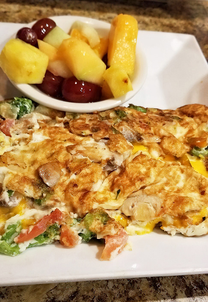 Behold the omelet in its natural habitat—perfectly executed, generously filled, and accompanied by fruit that didn't come from a can. This is breakfast royalty.