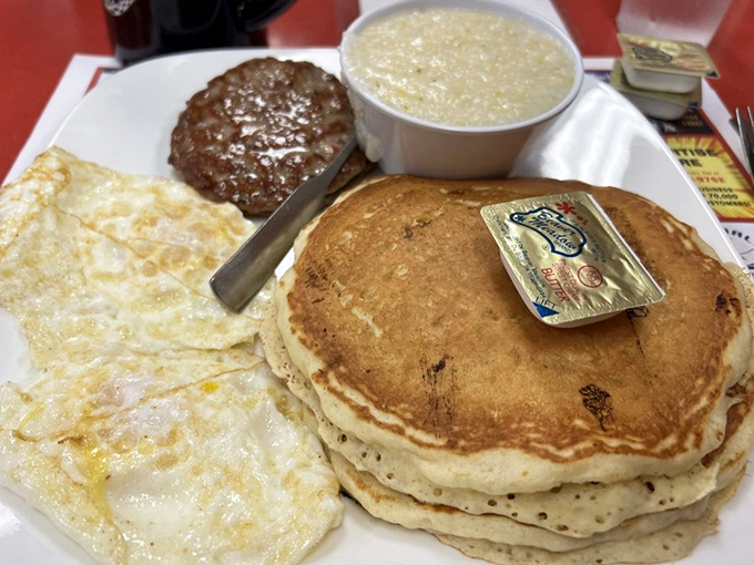 The holy trinity of breakfast perfection: golden pancakes stacked high, eggs sunny-side up, and a sausage patty that's been kissed by the griddle gods.