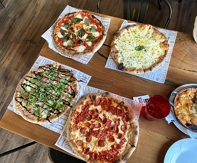 Pizza paradise on a wooden table. Four distinct pies that prove variety isn't just the spice of life&mdash;it's the whole meal.
