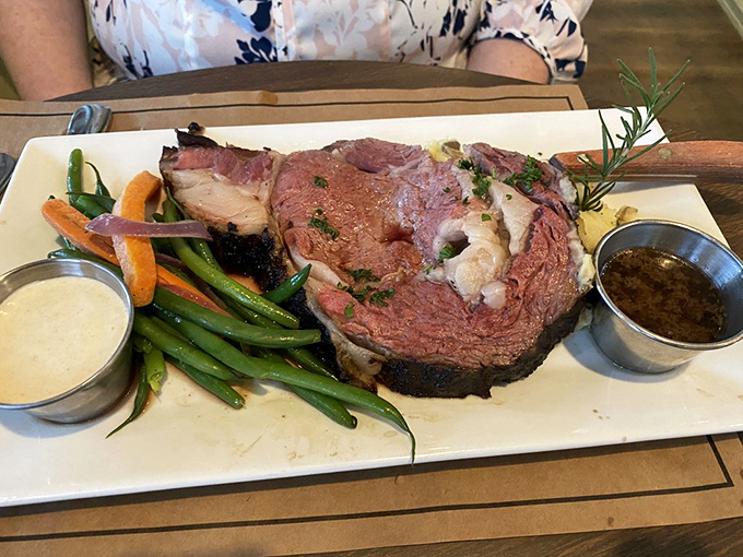 The star of the show arrives: prime rib cooked to pink perfection, accompanied by vibrant vegetables and twin sauces. Carnivore poetry on a plate.