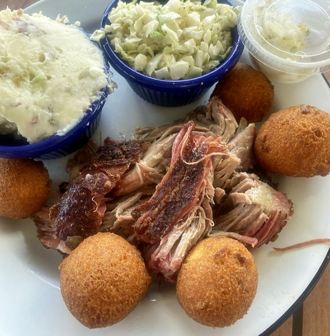 Barbecue nirvana on a plate: tender pulled pork with perfect bark, golden hushpuppies, creamy potato salad, and tangy slaw that dance together in smoky harmony.