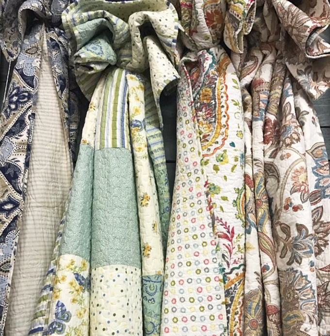 Quilted treasures hanging like fabric time capsules, each pattern telling stories of Sunday dinners and holiday gatherings.