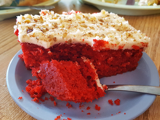 Behold the star attraction: red velvet cake so vibrant it could stop traffic, topped with cream cheese frosting that strikes the perfect balance between tangy and sweet.