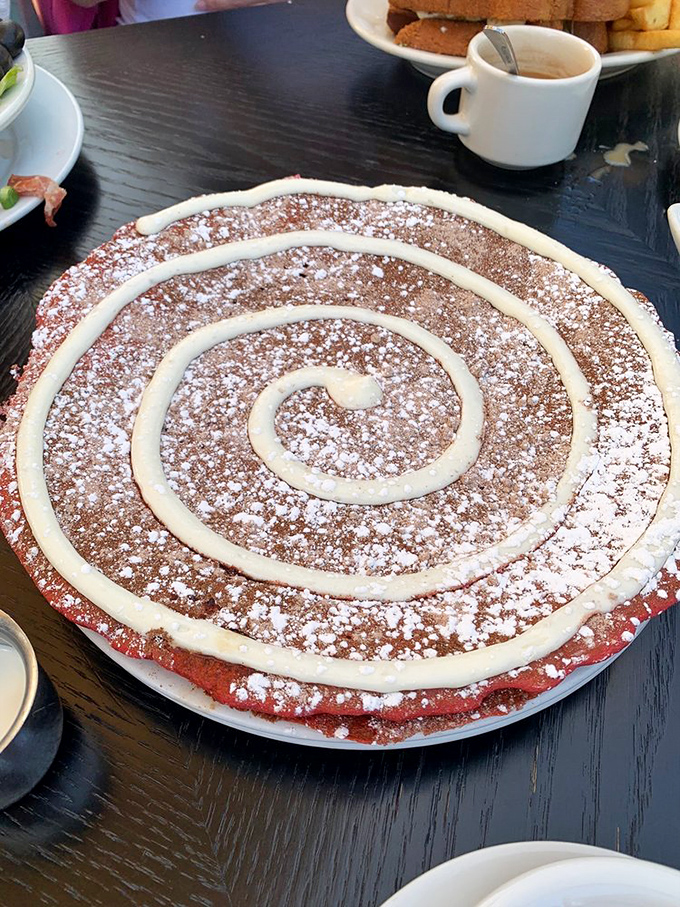 The Red Velvet pancake arrives like a dessert in disguise, wearing a spiral of cream cheese icing that would make any birthday cake jealous.