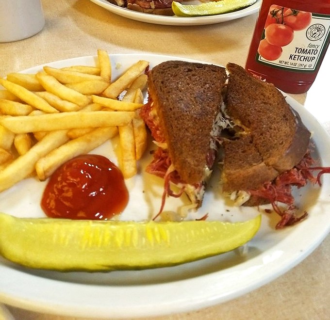 The legendary Reuben in its natural habitat&mdash;accompanied by crispy fries and a pickle spear. This isn't just a sandwich; it's architecture with sauerkraut.